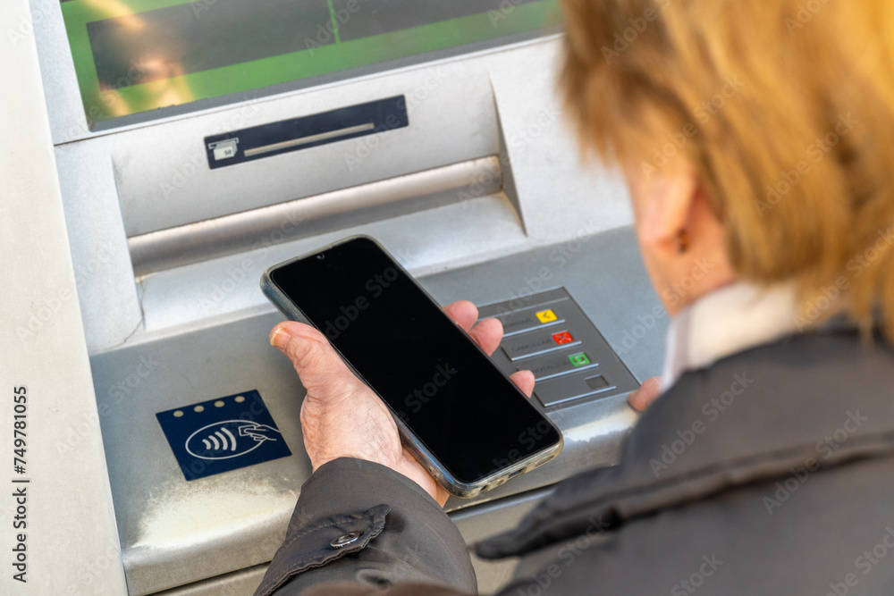 Older woman brings the phone to the ATM, NFC contactless communication ...