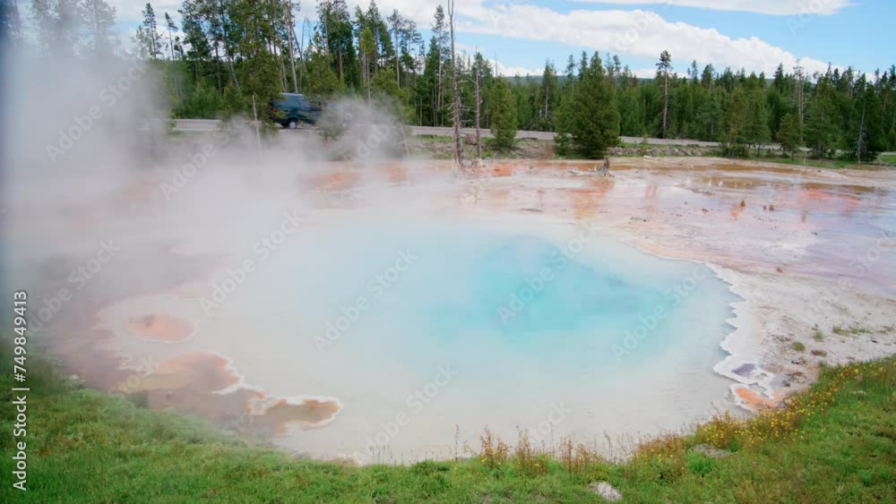 A vivid blue geothermal pool steams amid a colorful mineral-rich ...