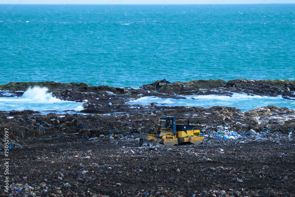 Garbage excavator pushing a pile of waste on coast, sea shoreline ...