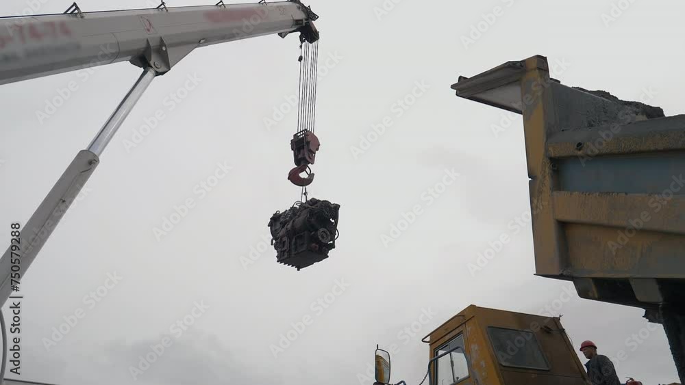 Industrial crane lowering the heavy machine engine closer to the ground ...