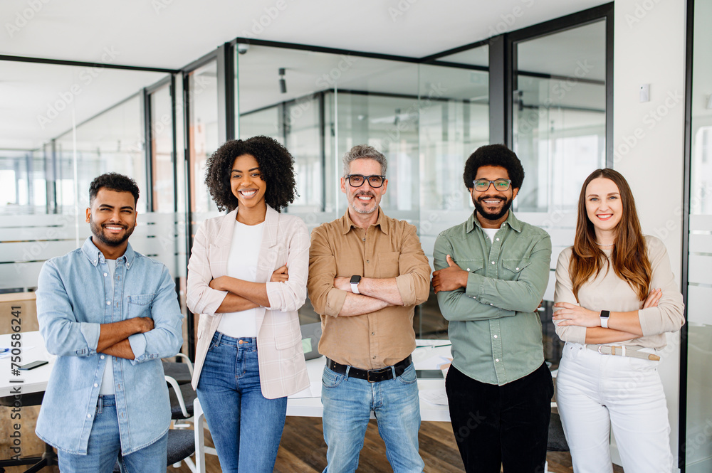 A vibrant team of five professionals stands with confidence in office ...