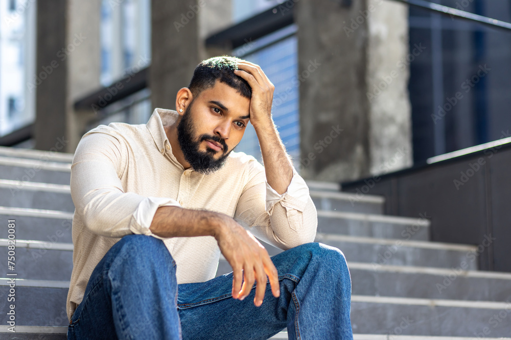 Upset and disappointed young Indian man sitting on the steps of an ...