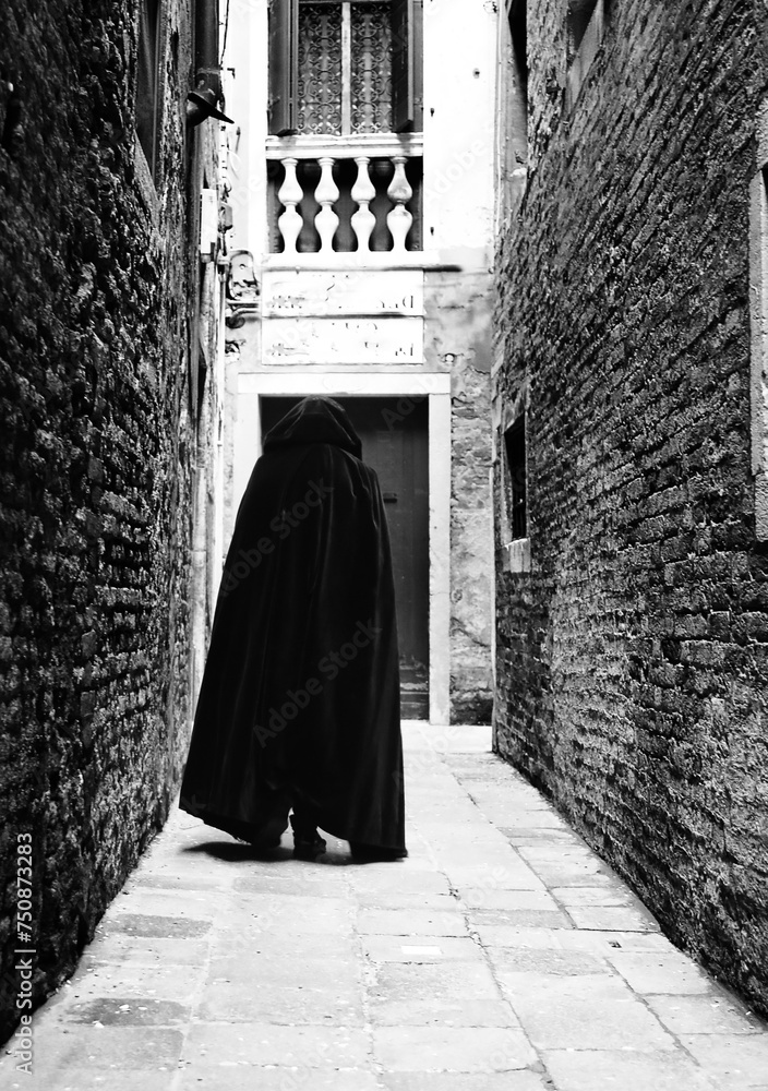 hooded person with dark cloak walking in city alley with effect in ...