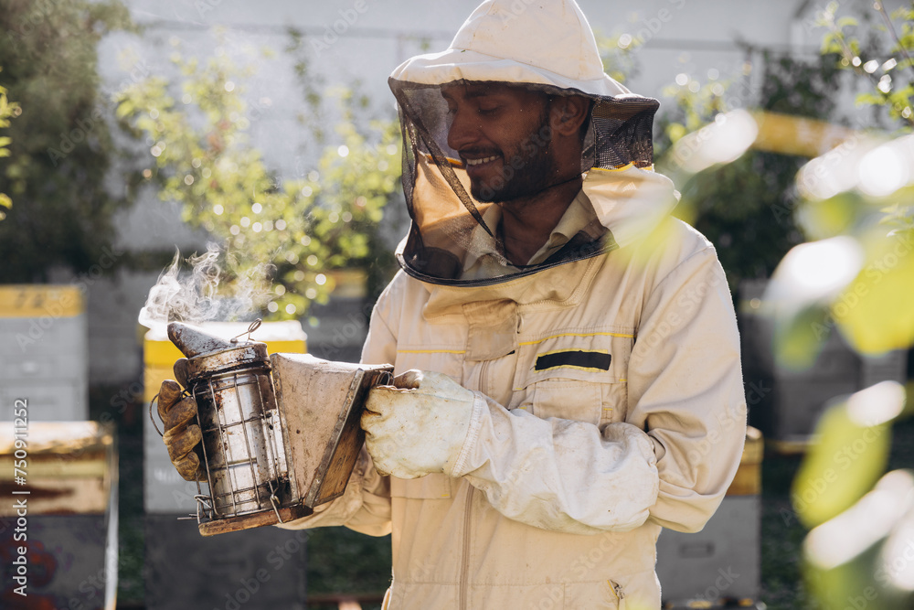 Happy smiling Indian male Beekeeper smoking honey bees with bee smoker ...