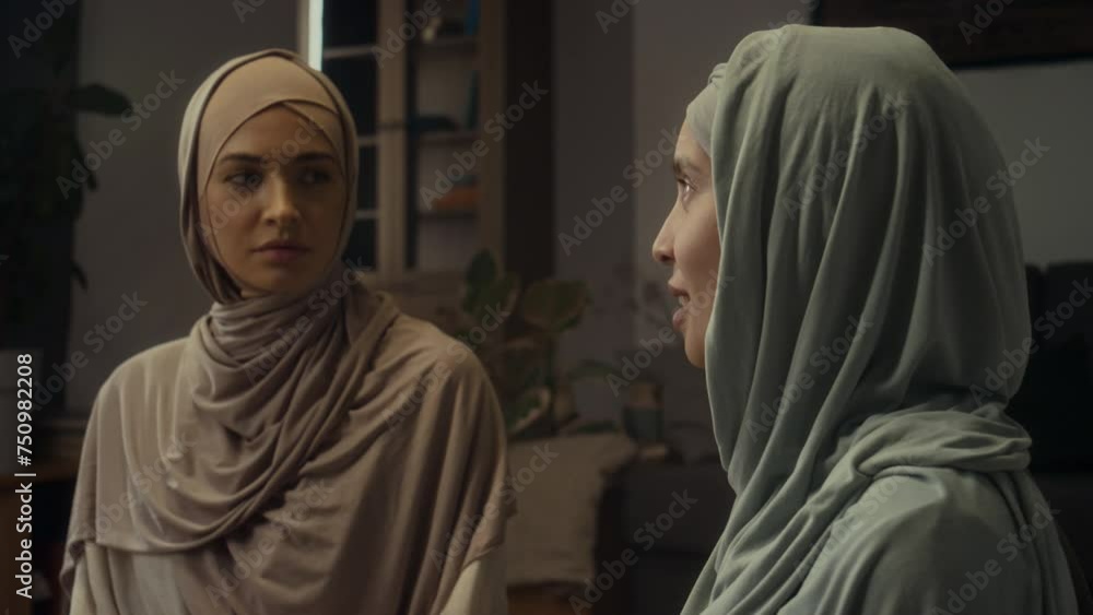Side tilt footage of two sisters in hijabs and abayas sitting on floor ...