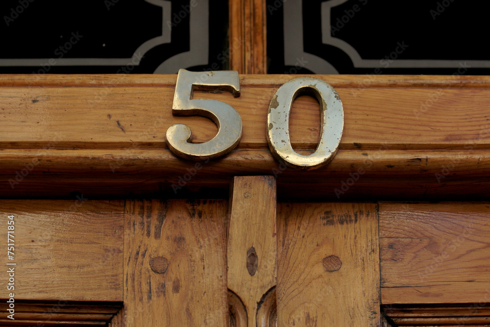 House number 50 with the fifty in bronze on a black wooden front door ...