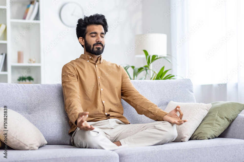 Calm middle eastern man sitting on pillowed sofa in siddhasana position ...
