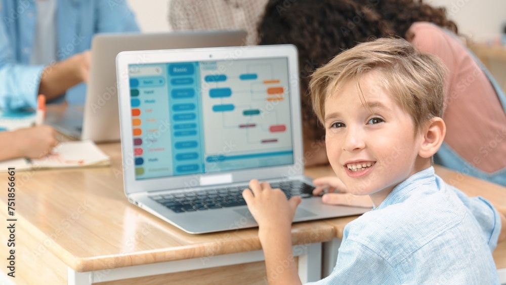Smart caucasian boy looking at camera in STEM technology class while group of diverse student ...