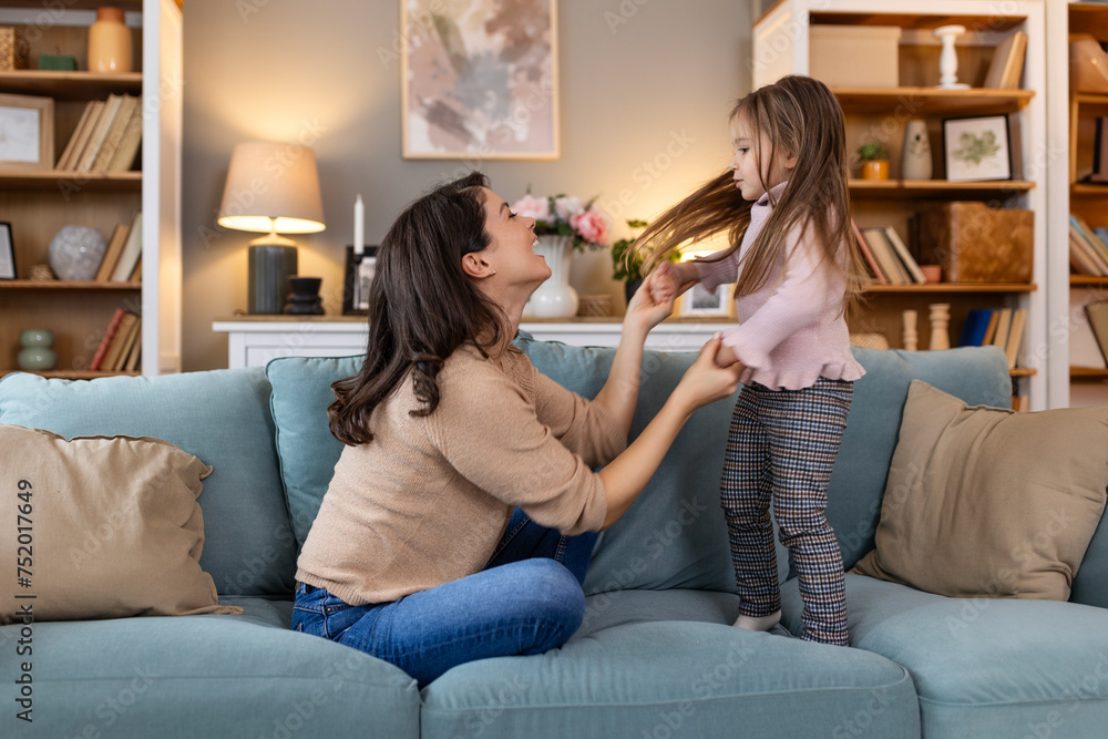 Cheerful caring mom holding adorable little kid daughter in arms, hugging girl with check touch ...