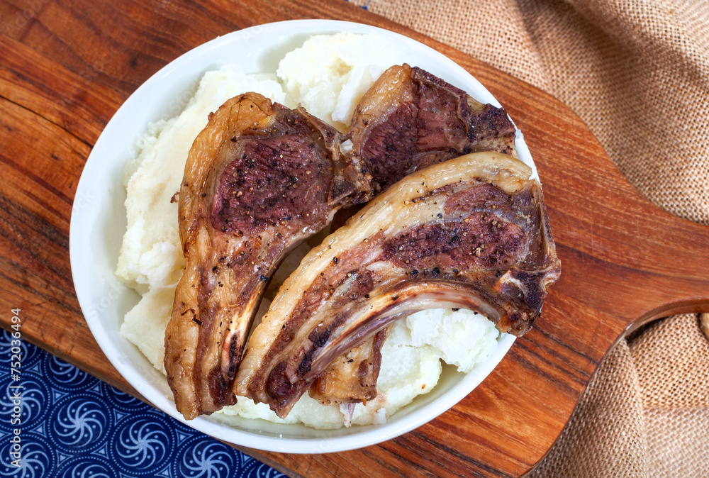 three lamb rib chops with pap or maize meal on rustic chopping board ...