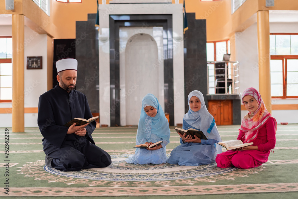 A Muslim teacher teaches children girls to read a holy book Quran ...