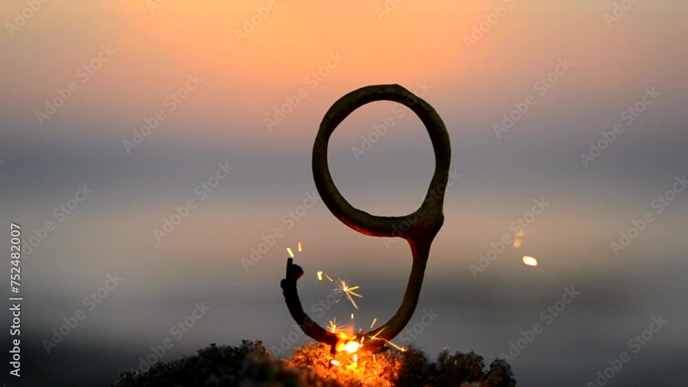 Sparkler in shape of number nine 9 burning against backdrop of sea ...