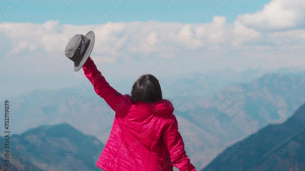 Girl removing hat and stretch arms while standing against mountains at ...