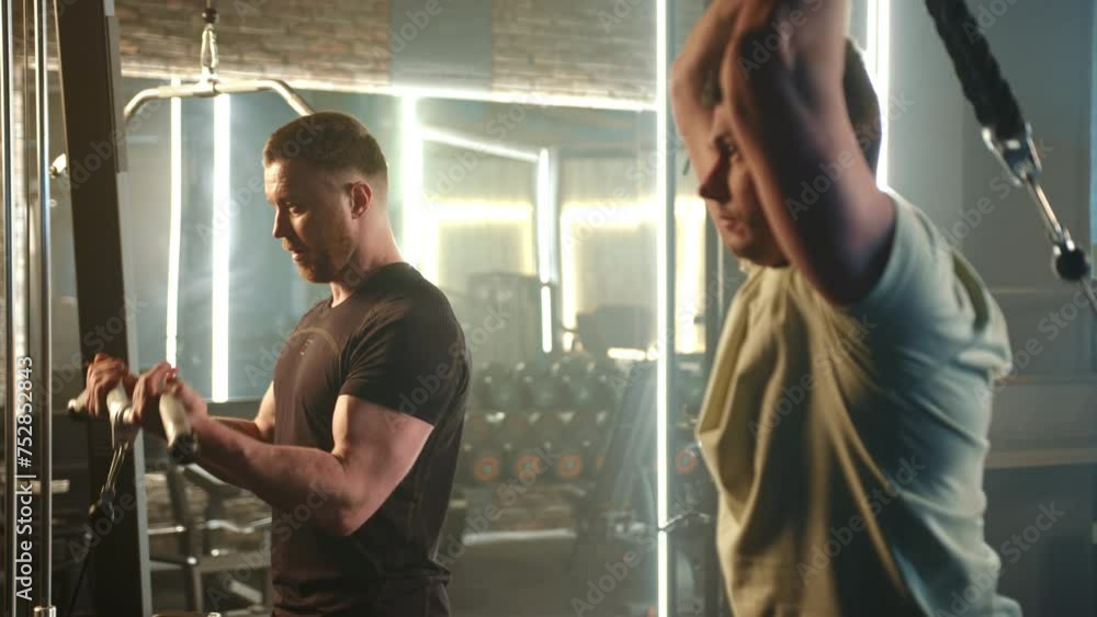 In the well-equipped gym, two focused men are simultaneously using the ...