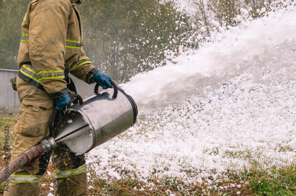 A firefighter in protective clothing extinguishes a fire with foam. A ...