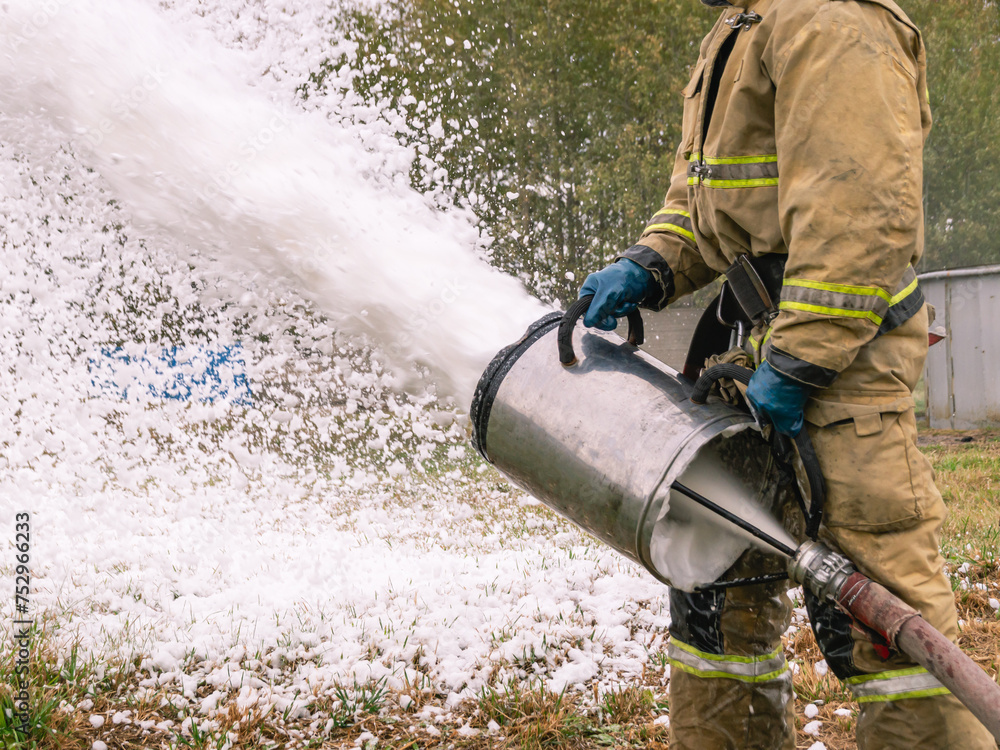 A firefighter in protective clothing extinguishes a fire with foam. A ...
