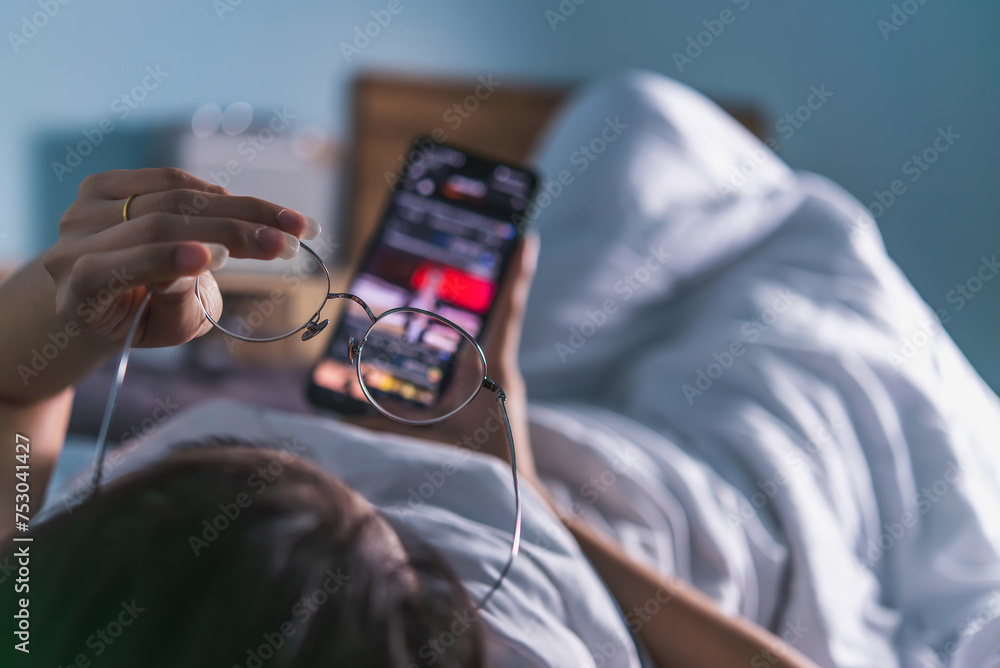 An over-the-shoulder view of a person in bed checking a smartphone with ...