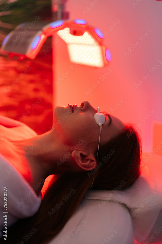 Vertical shot of young woman having red LED light facial photodynamic ...