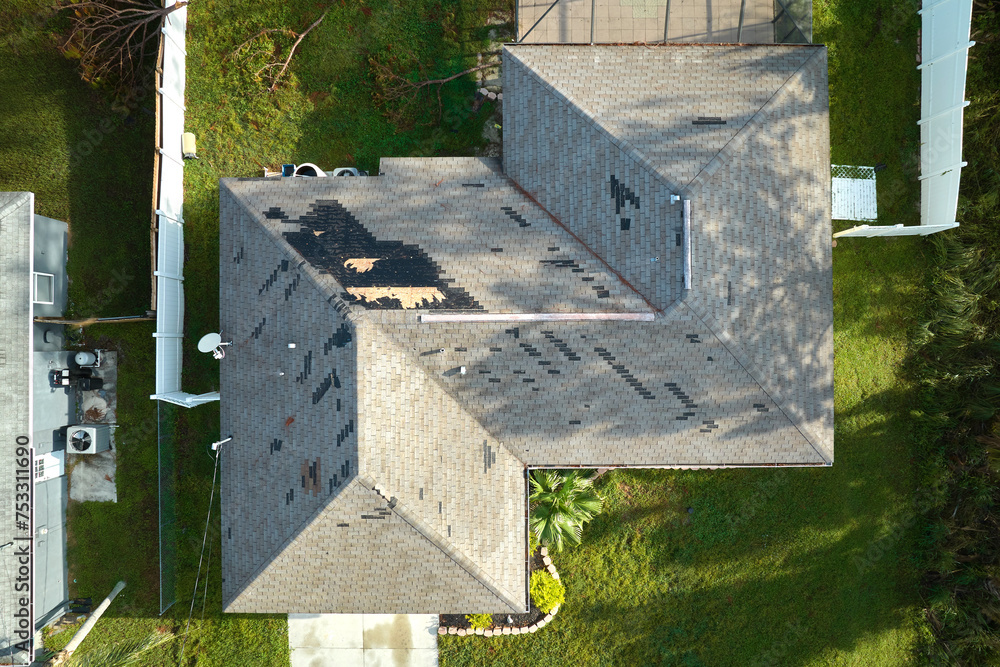 Wind damaged house roof with missing asphalt shingles after hurricane ...