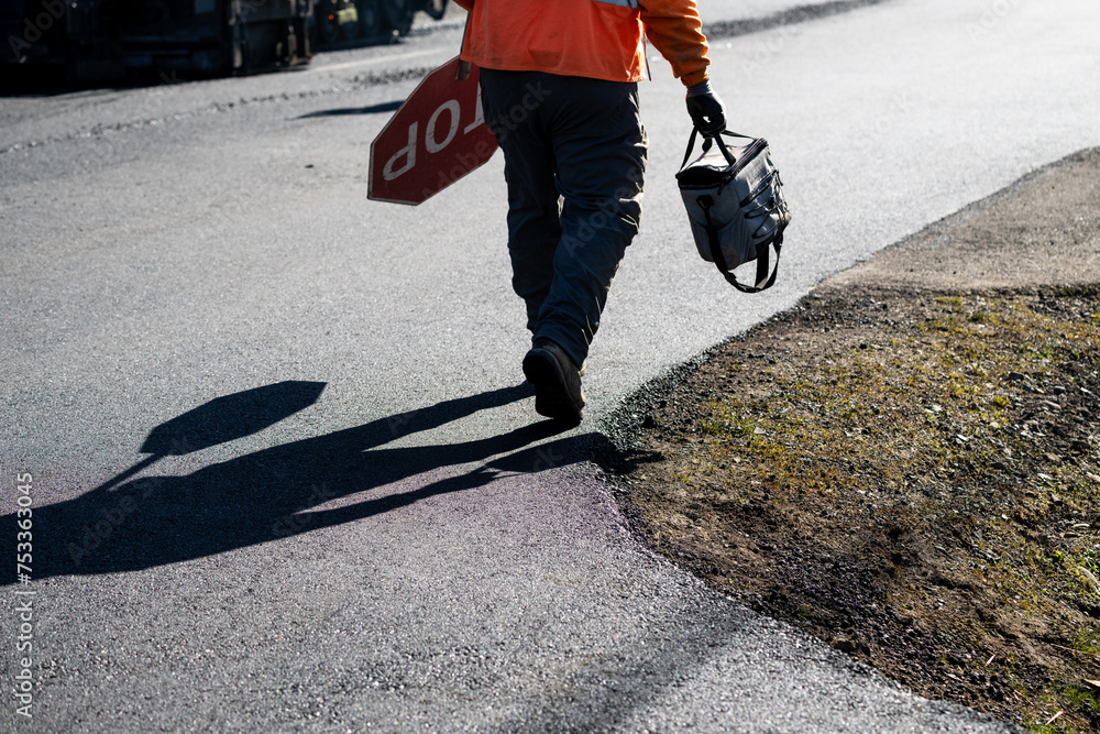 Road construction worker flagger walking with temporary stop sign and ...