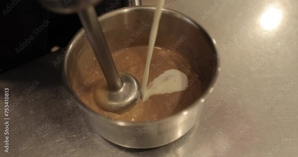 Female hands grind ingredients in a metal pot with an immersion blender ...