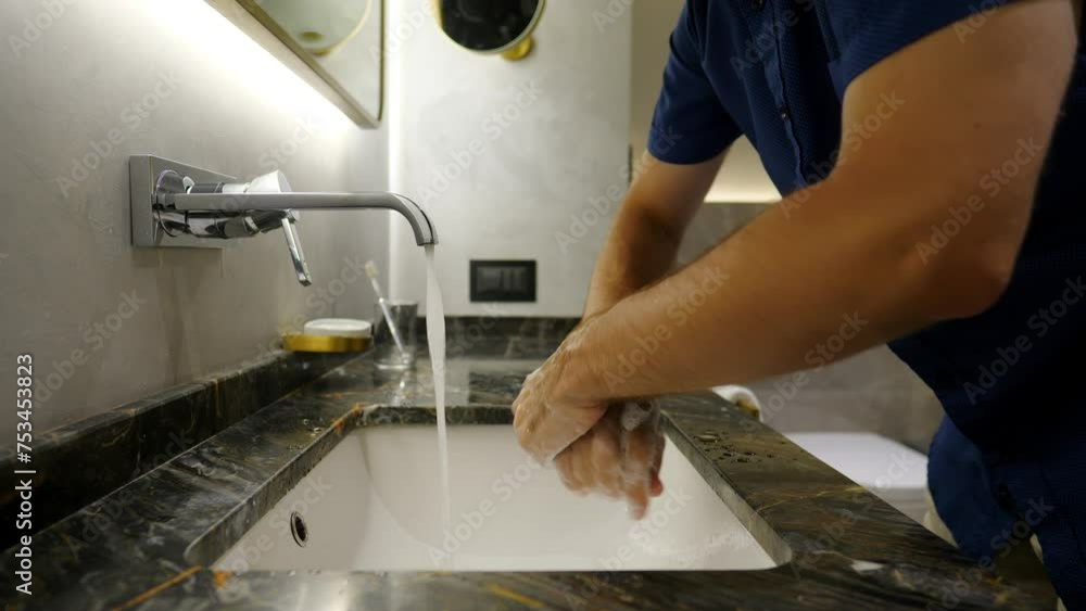 Man stands by sink in modern bathroom, diligently washing his hands ...