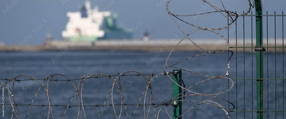 PROTECTING SITE - Seaport fence with razor wire and LNG tanker sailing ...