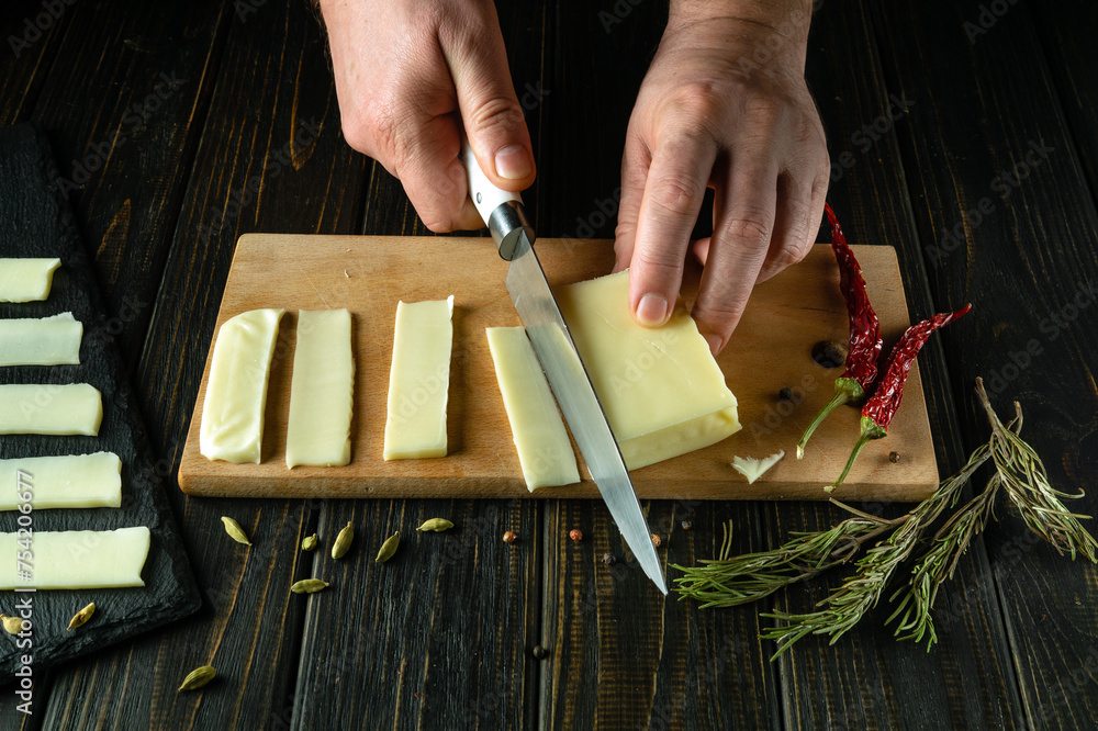 Chef's hands use a knife to cut Mozzarella cheese into small pieces for ...