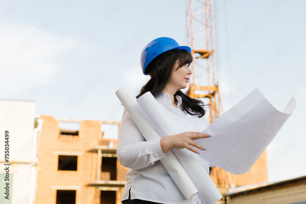 Plus size female engineer in a white shirt and blue helmet is holding ...