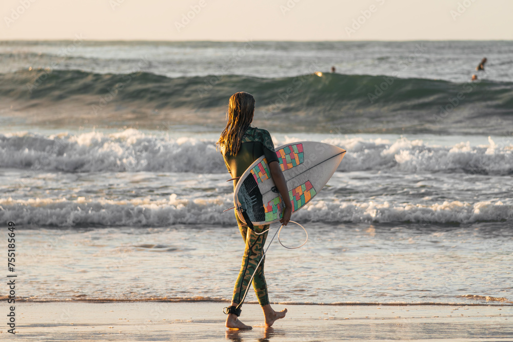 Young surfer girl in camo wetsuit entering the sea with her surfboard ...