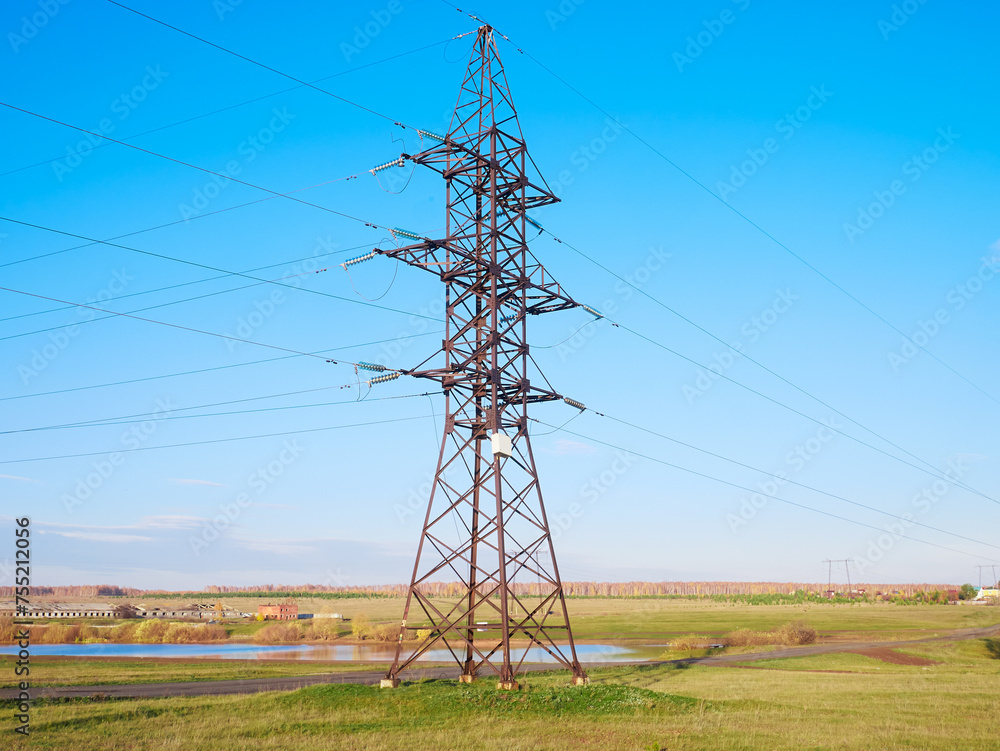Metal power tower with high-voltage cables against the green field and ...