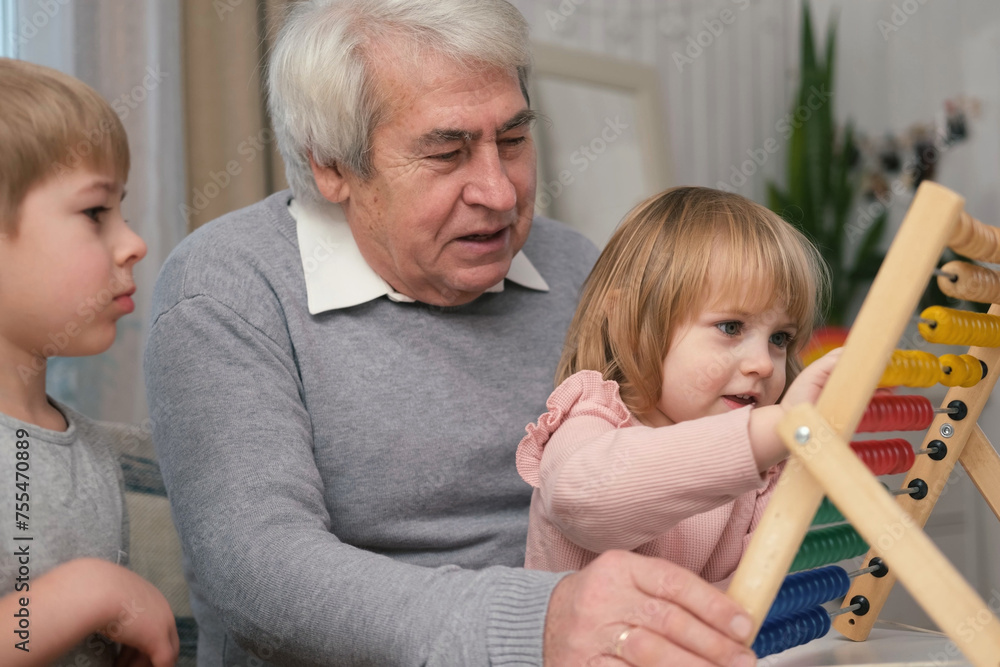 Grandfather playing toys with grandson and young granddaughter indoor ...