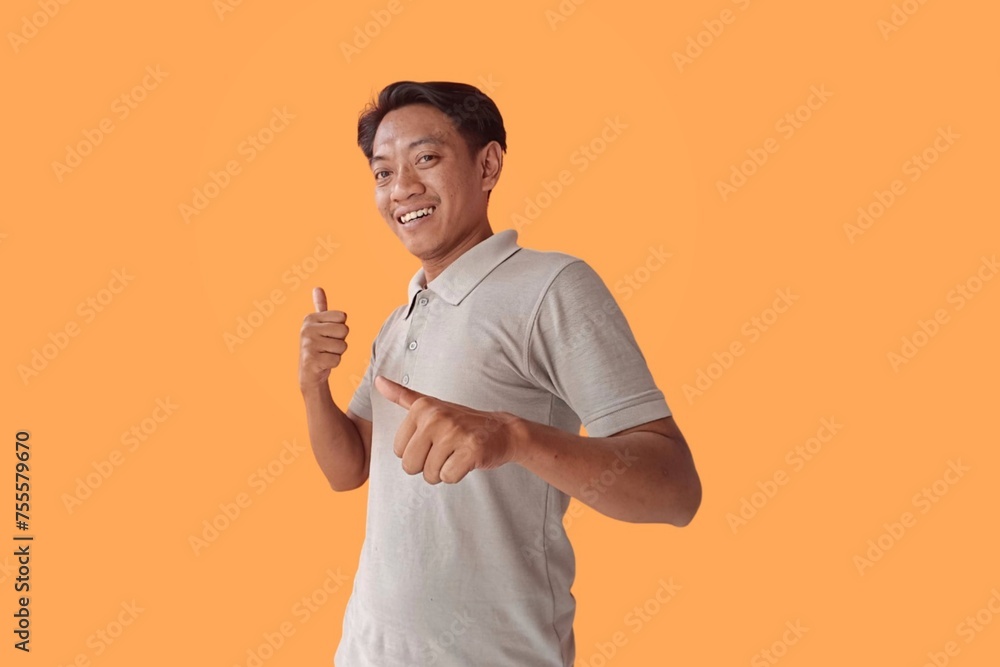 Handsome Asian man standing over orange background pointing to the back ...