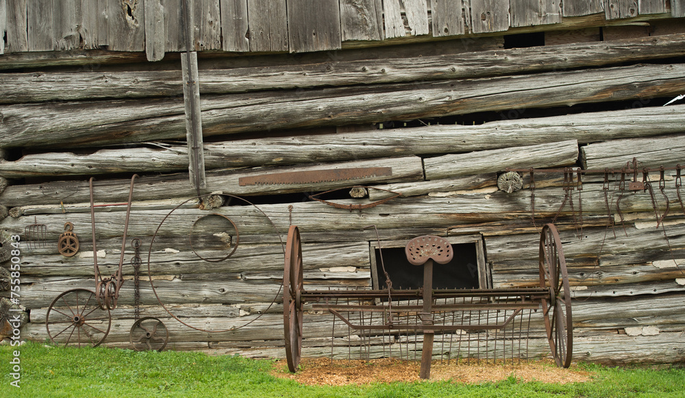 Old antique rustic rusty farm machinery in front of log cabin exterior ...