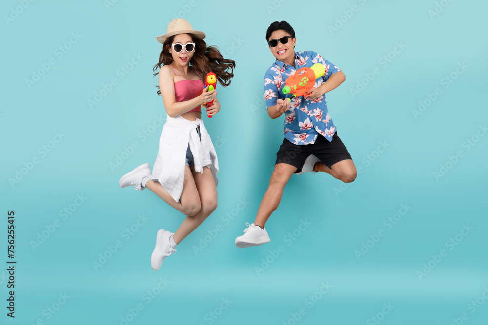Happy Asian couple jumping and using water guns on blue background ...