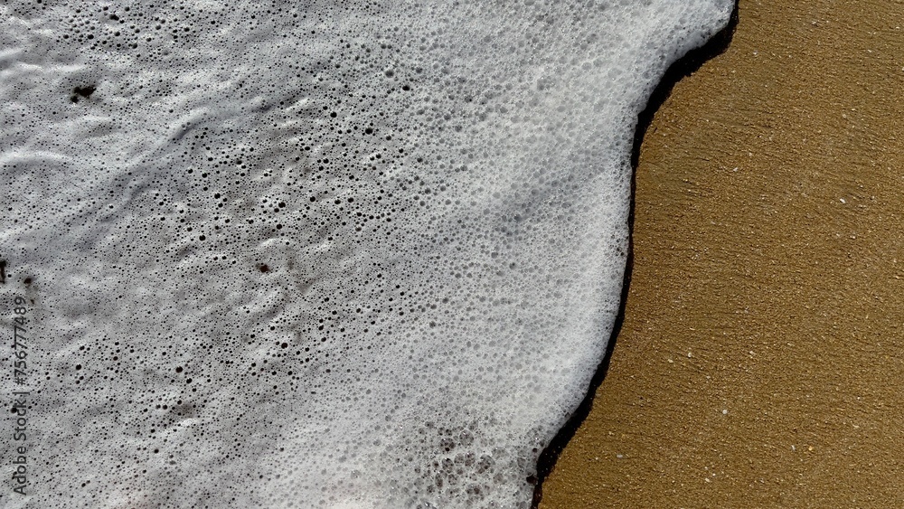 Sea foam on sandy beach, as ocean wave washes up on the shore. Detail ...