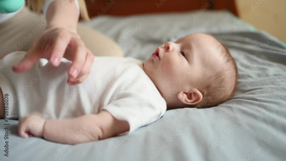 Cute baby is lying on bed, babbling. Mom gives baby a rattle in his ...