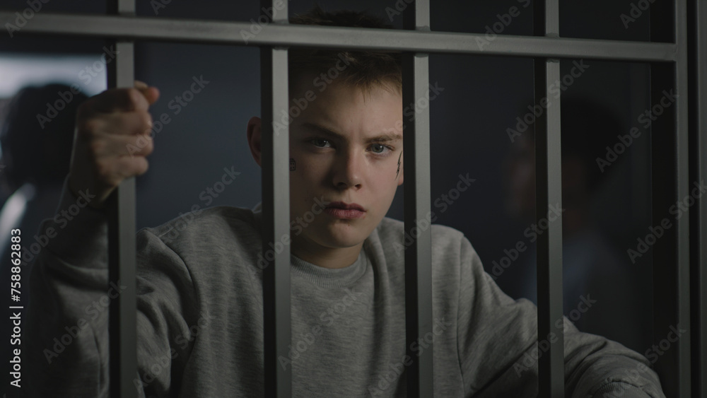 Caucasian teenager with face tattoos stands in prison cell in jail ...
