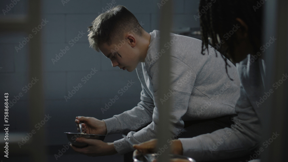 Diverse young prisoners eat disgusting prison food from iron bowls ...