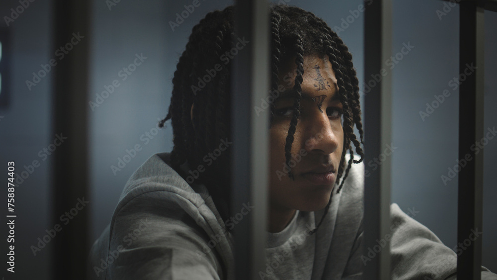 Angry African American teenage prisoner with face tattoos stands in ...