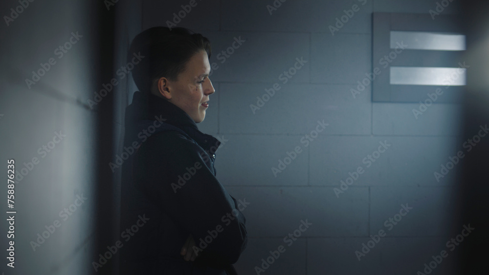 Teen prisoner leans on wall of jail cell and smiles. Teenager serves ...