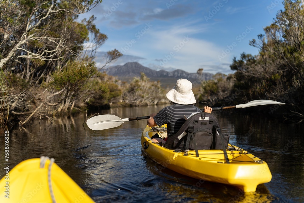 kayaking up a river in a canoe with mountains in a wilderness in a ...