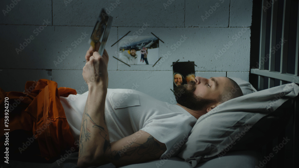 Male prisoner in orange uniform lies on bed in prison cell, looks at ...