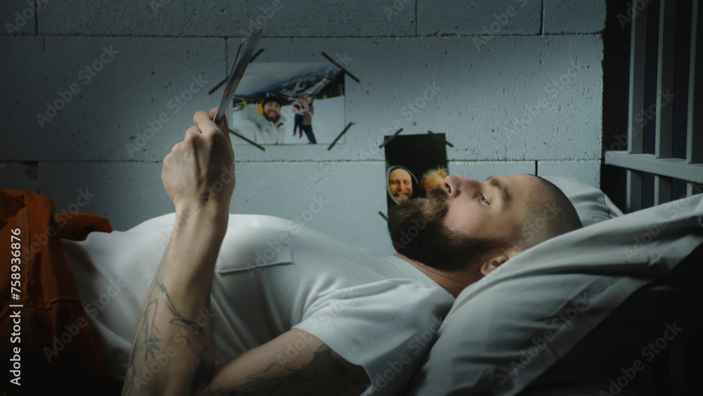 Male prisoner looks at photos lying on bed in prison cell. Pictures ...