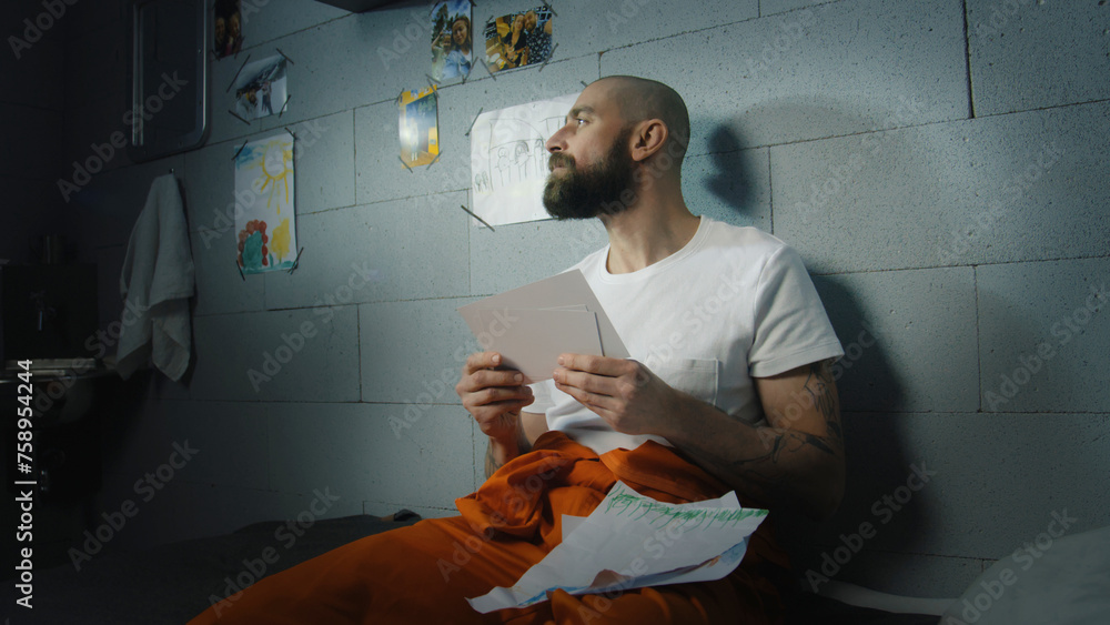 Upset male prisoner looks at family photos and kids drawings sitting on ...