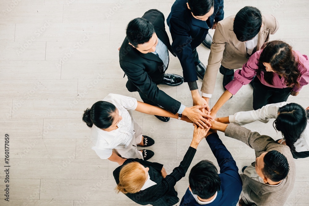 A top view shows four diverse businesspeople forming a circle stacking ...