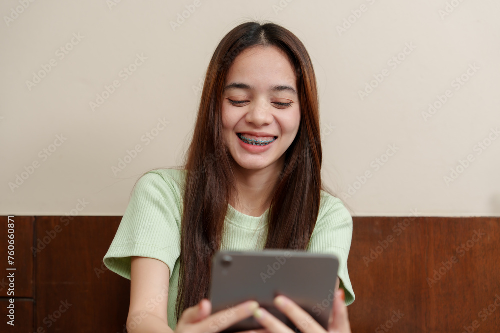 Engrossed young Asian lady with vibrant smile browses on tablet, casual ...