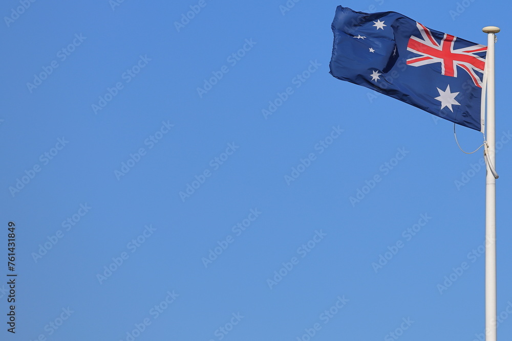 The Australian flag flying in the wind against a uniform clear blue sky ...