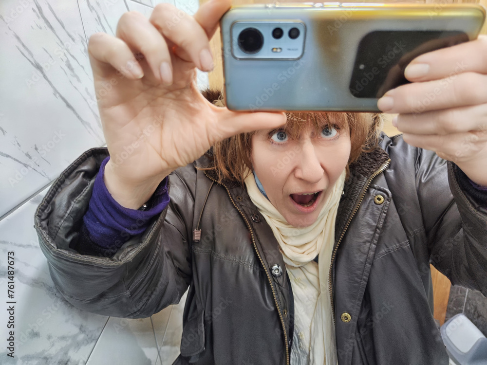 Mature woman captures her reflection while taking a selfie. The ...