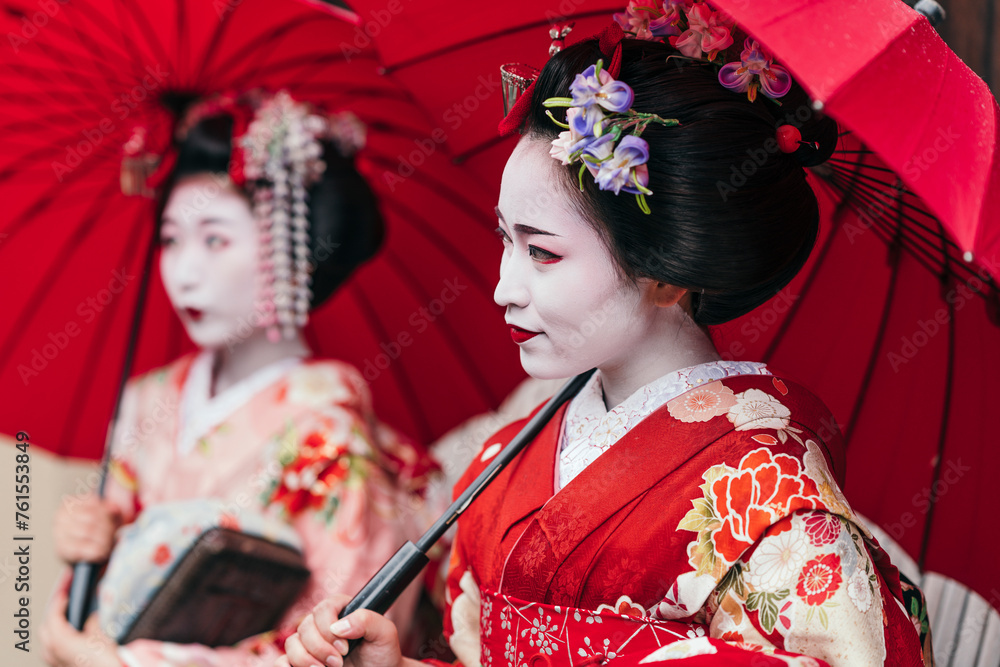 Maiko Geisha adorned in a traditional red kimono stands gracefully ...